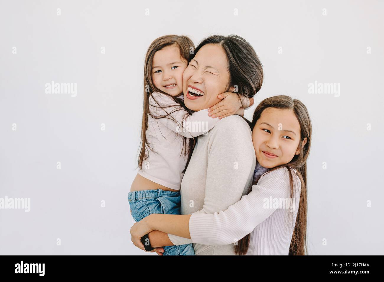 Cute daughters embracing happy mother by white background Stock Photo ...