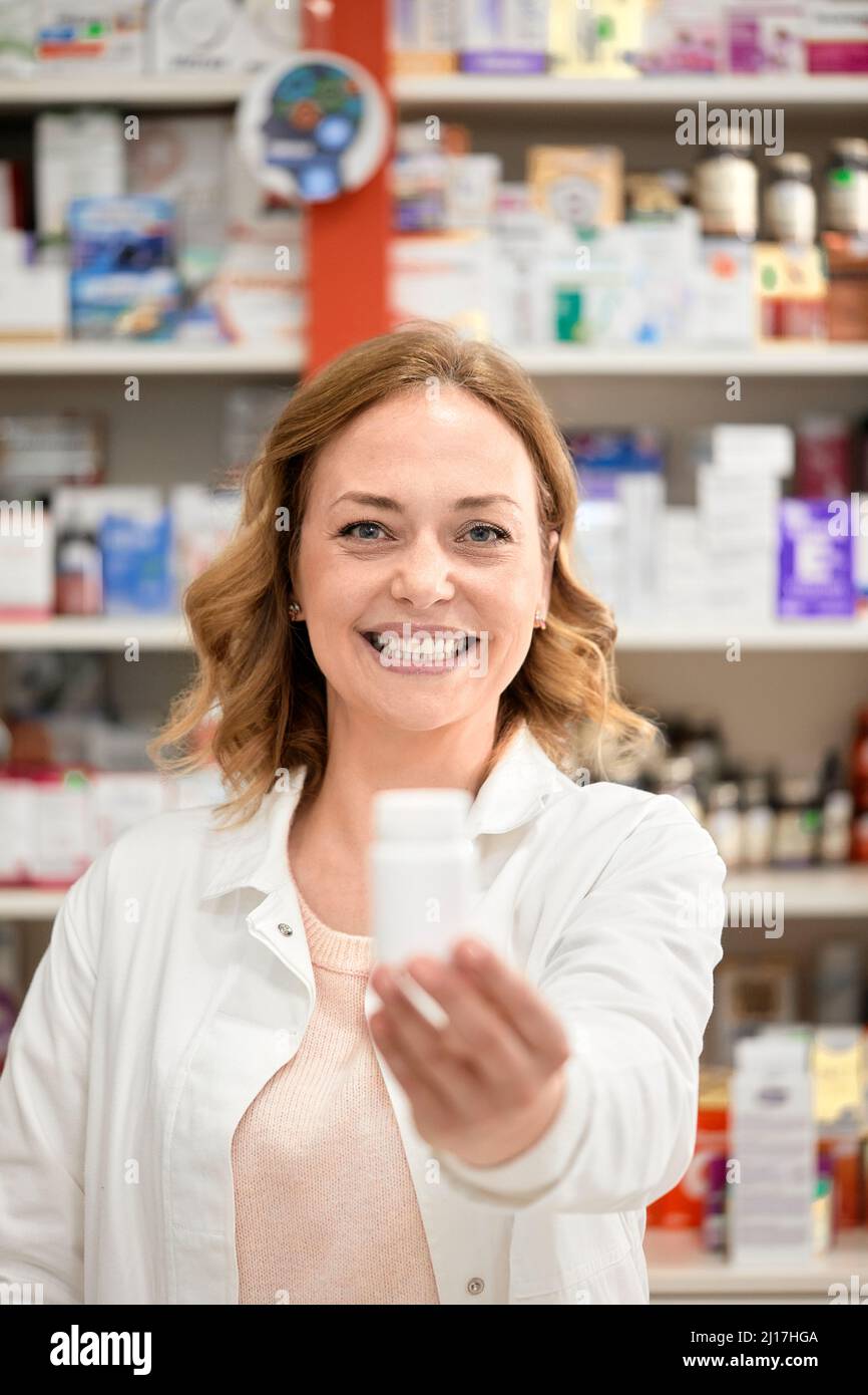 Happy pharmacist giving bottle of medicine standing in pharmacy store ...