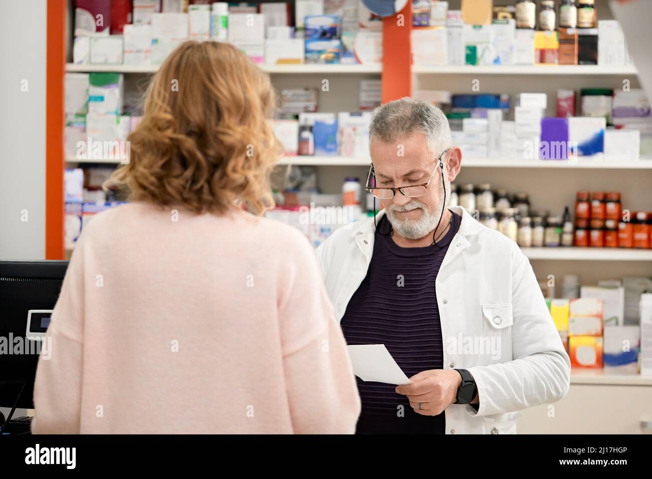 Pharmacist reading prescription standing with customer at checkout ...