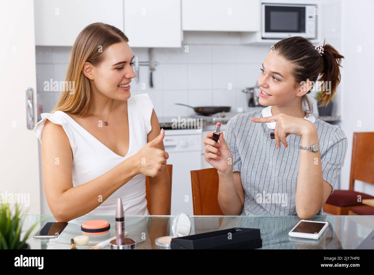 Two modern girls friends having conversation and applying cosmetics in ...