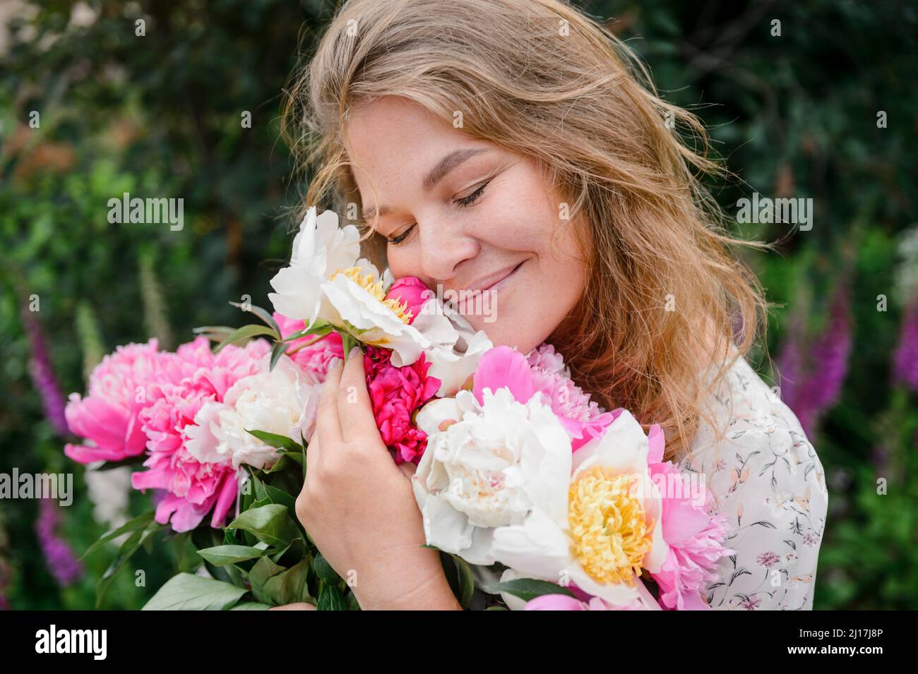 Smiling blond woman with eyes closed hugging flowers Stock Photo - Alamy