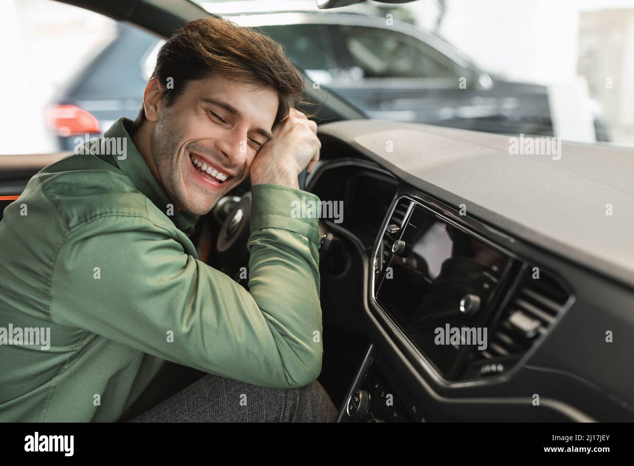 Delighted young man sitting in driver's seat, hugging steering wheel of ...