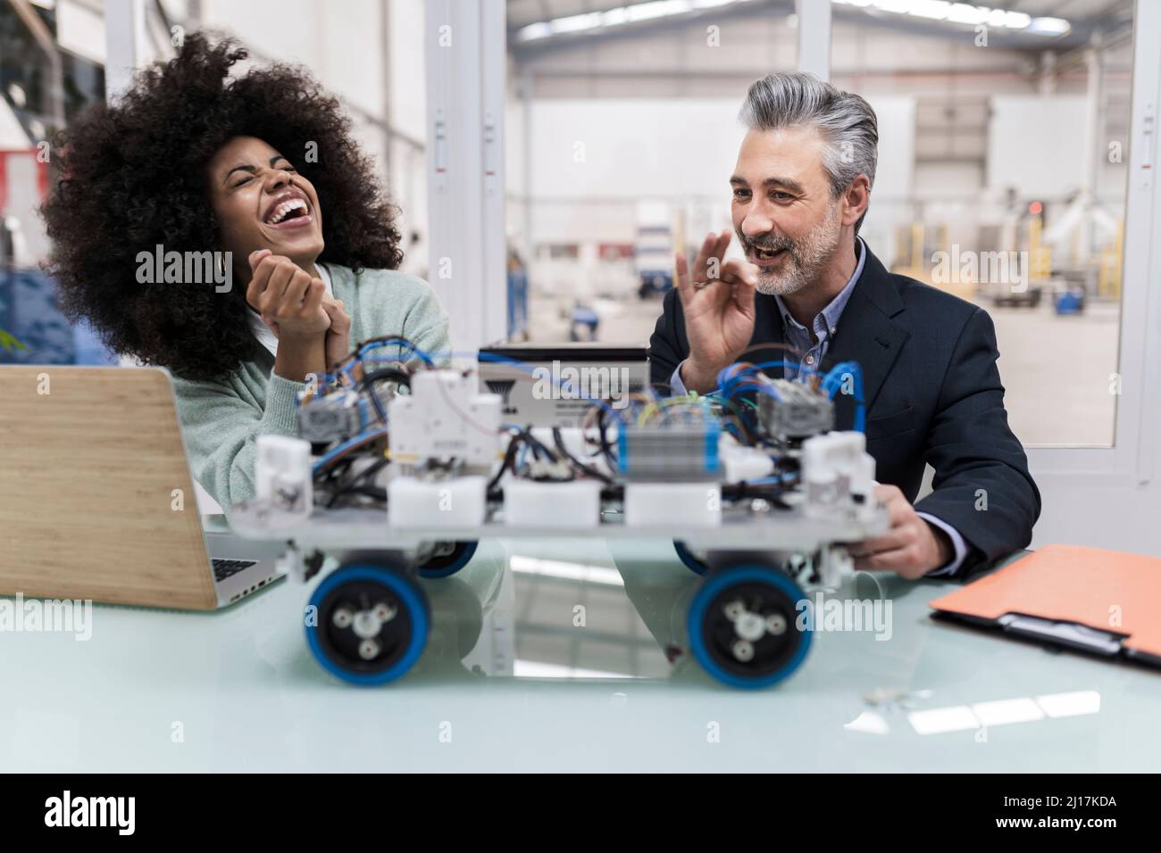 Happy engineers discussing robotic vehicle in factory Stock Photo - Alamy