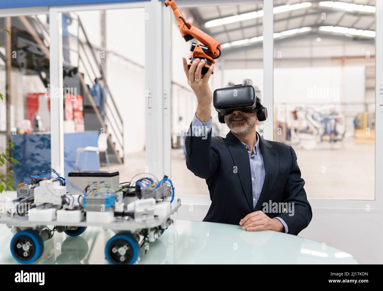 Smiling businessman wearing virtual reality holding robotic arm model ...