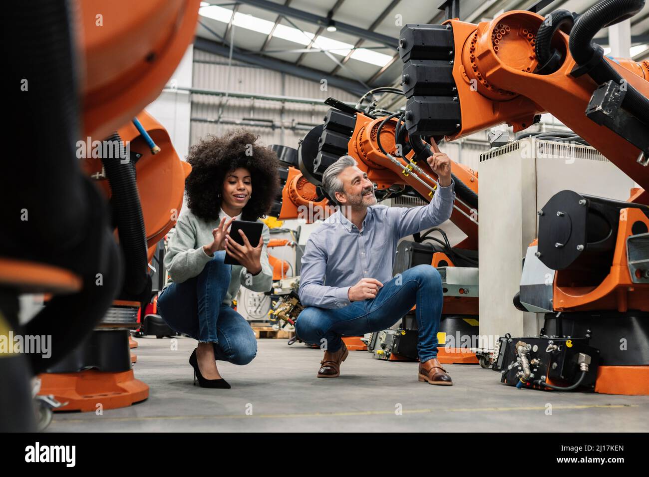 Engineer using tablet PC sitting by developer pointing robotic arm in ...