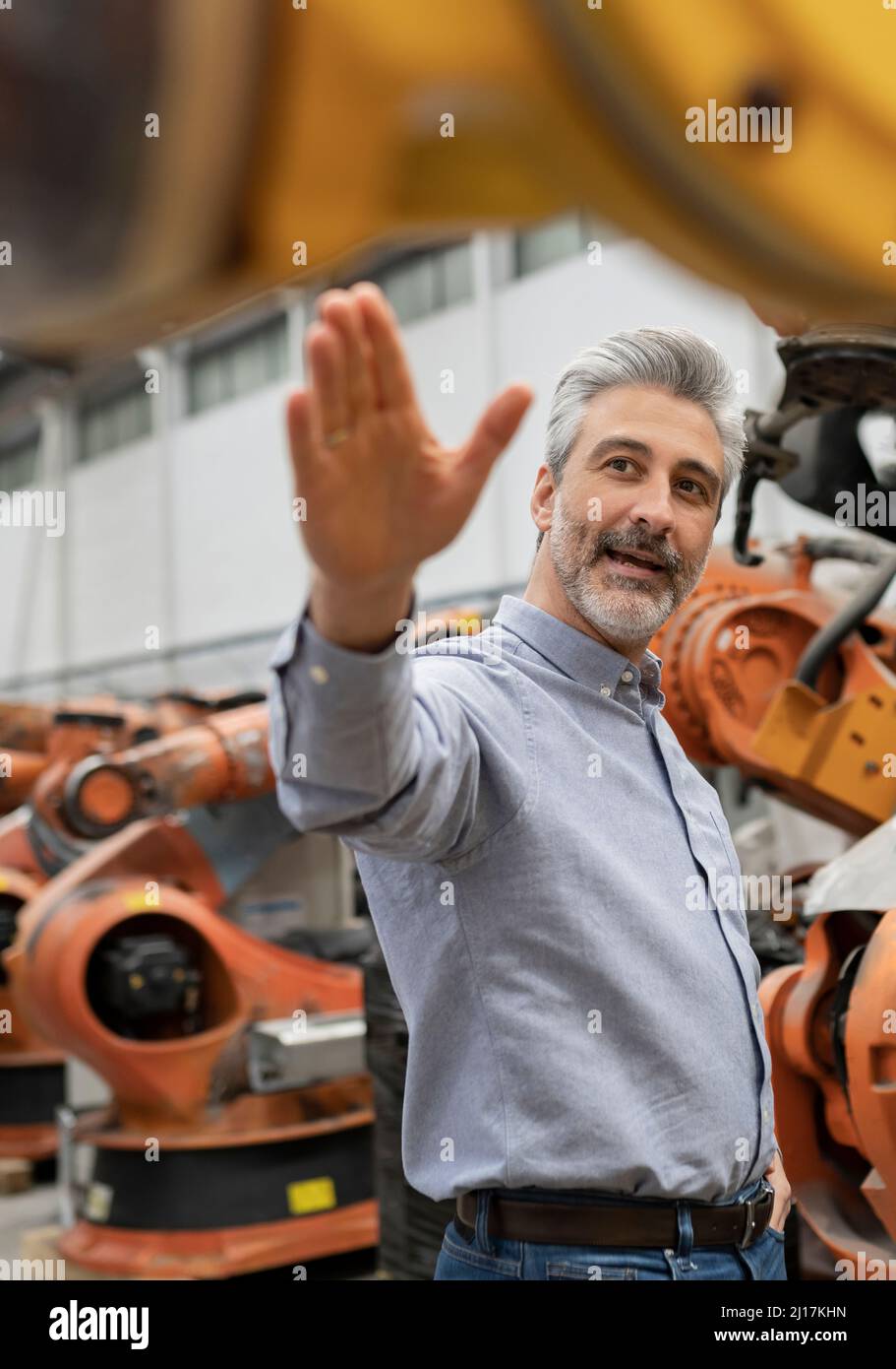 Engineer with gray hair showing machine standing in factory Stock Photo ...