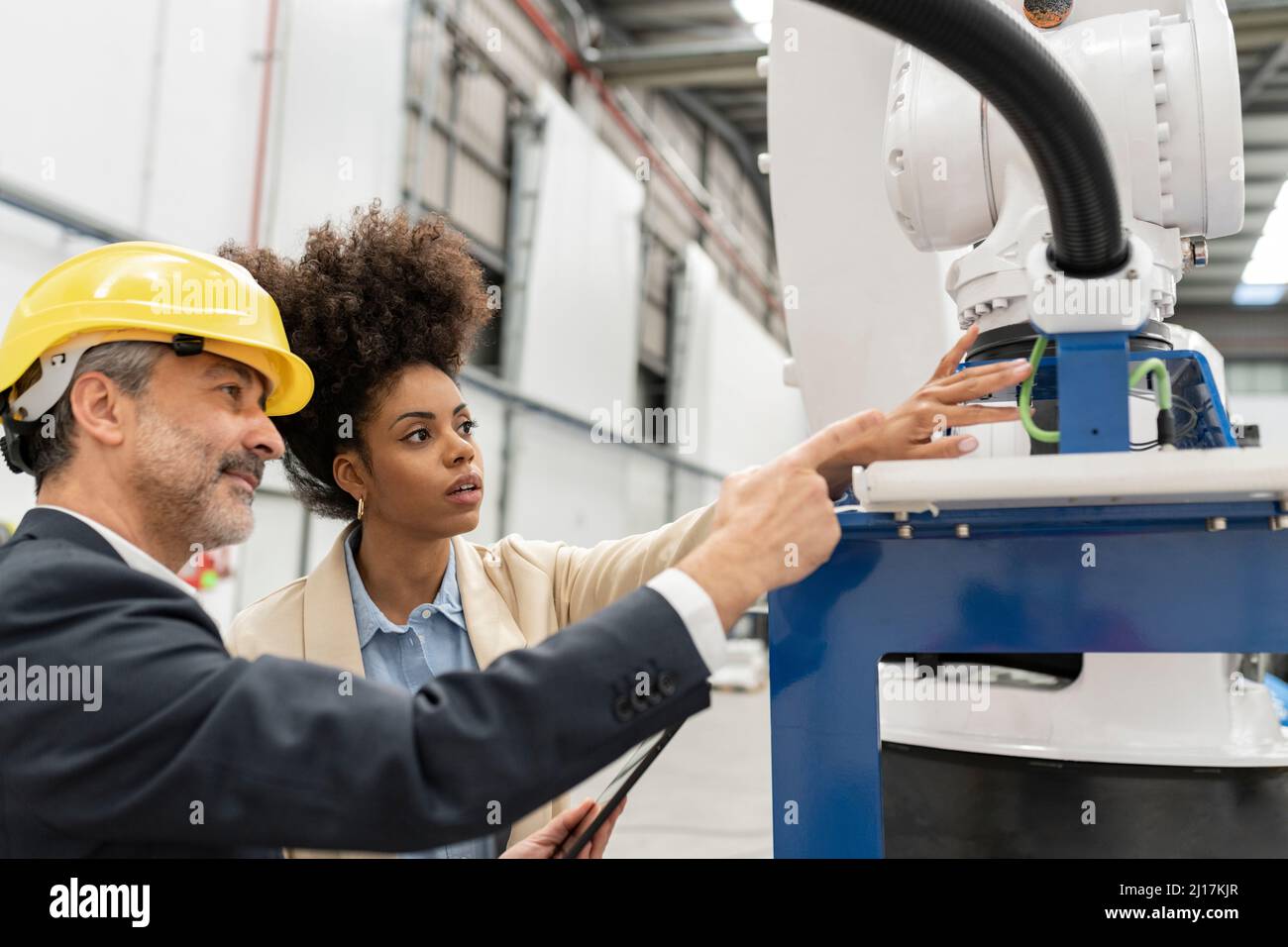 Technician analyzing robotic arm standing by engineer in factory Stock ...