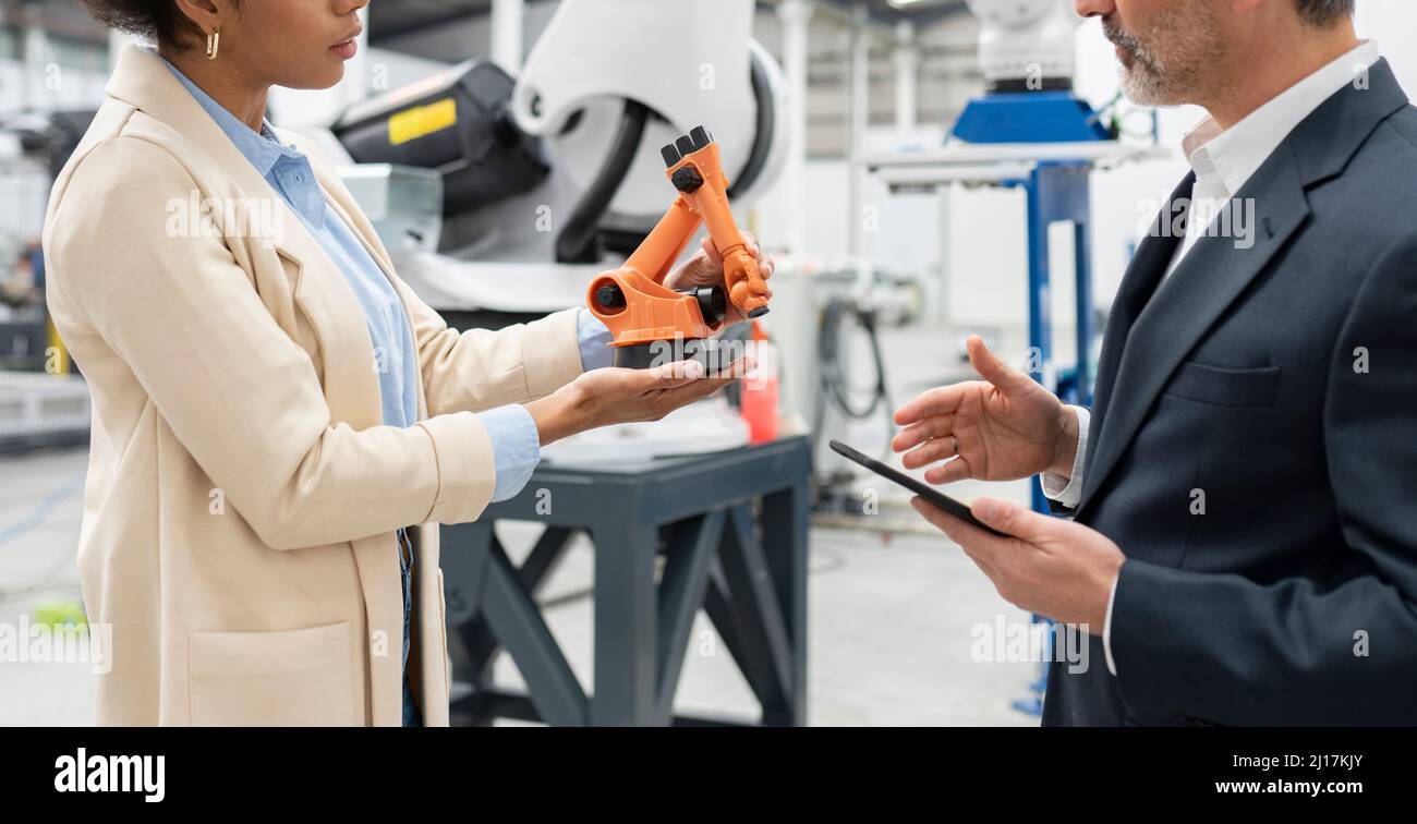 Developer showing model of robotic arm to businessman in factory Stock ...