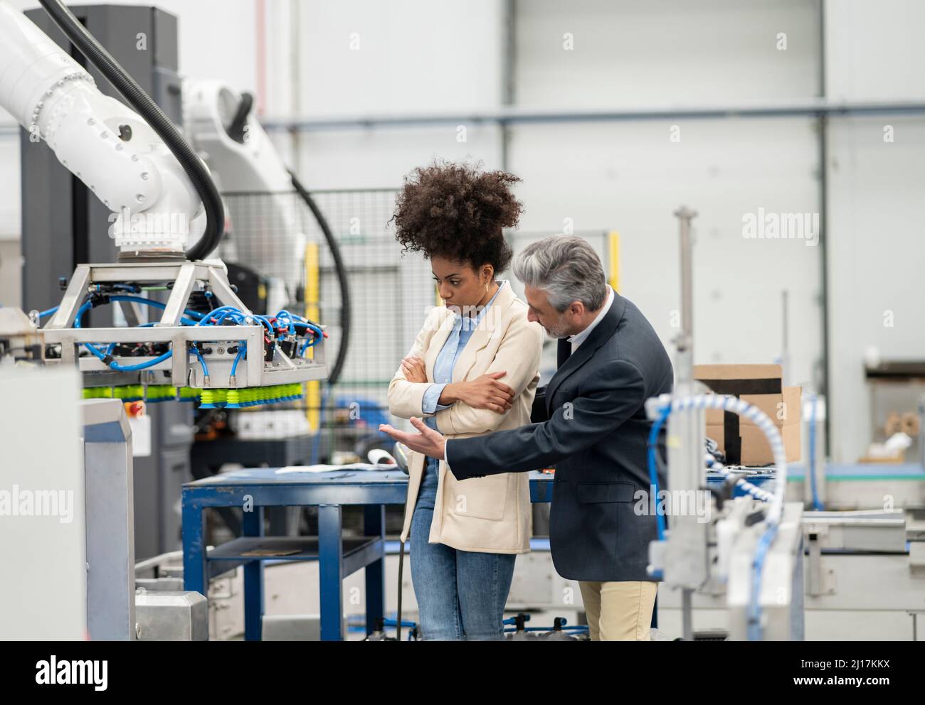 Engineer explaining robotic arm to developer standing with arms crossed ...