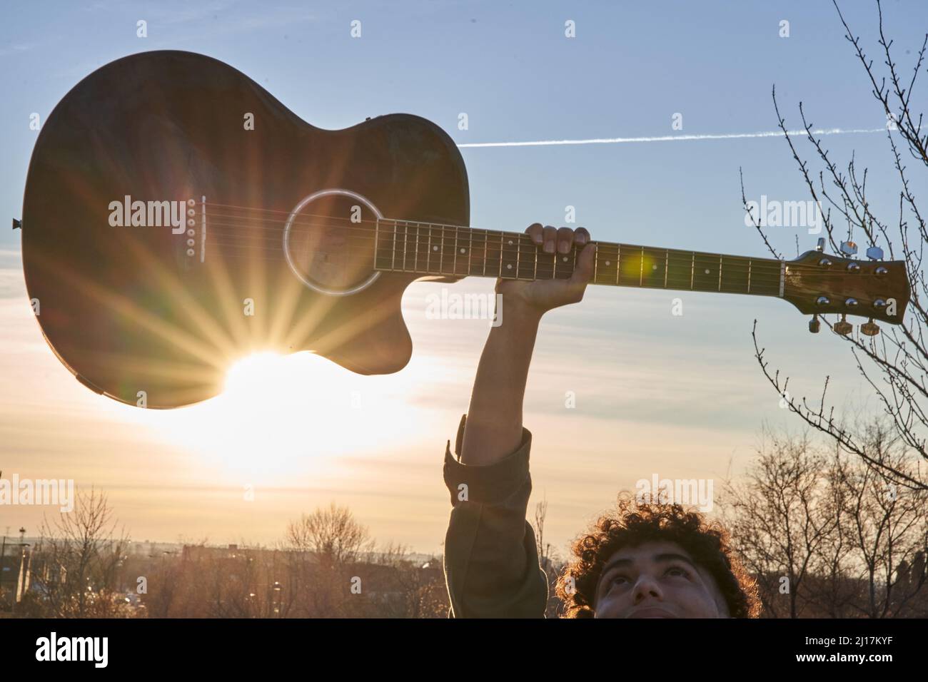 Man with a happy face holding a guitar above his head at sunset ...
