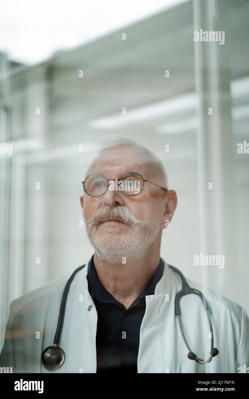 Thoughtful doctor with mustache wearing eyeglasses at medical clinic ...