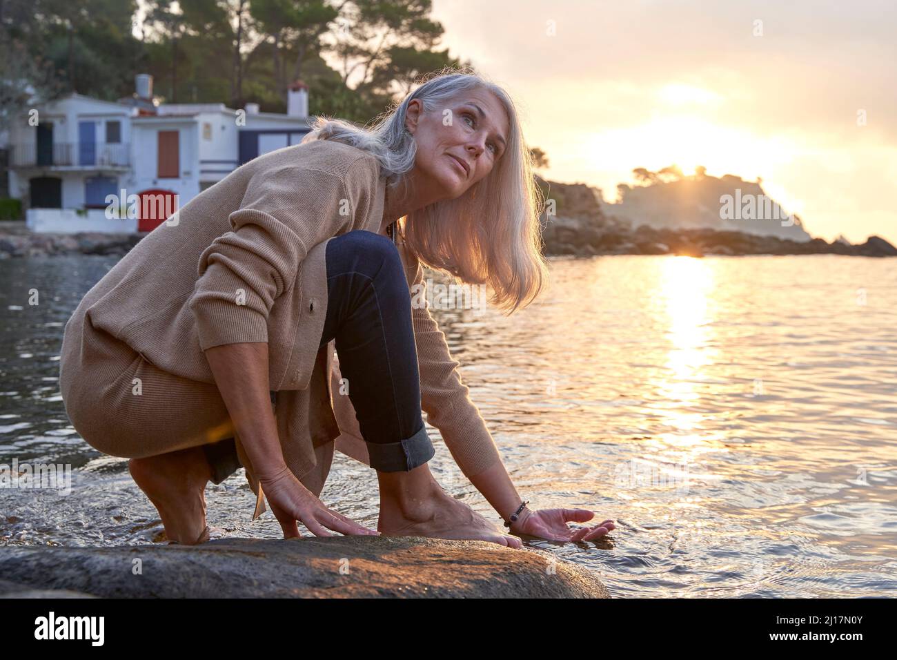 Gray haired woman dipping hand in water on rock at beach Stock Photo ...