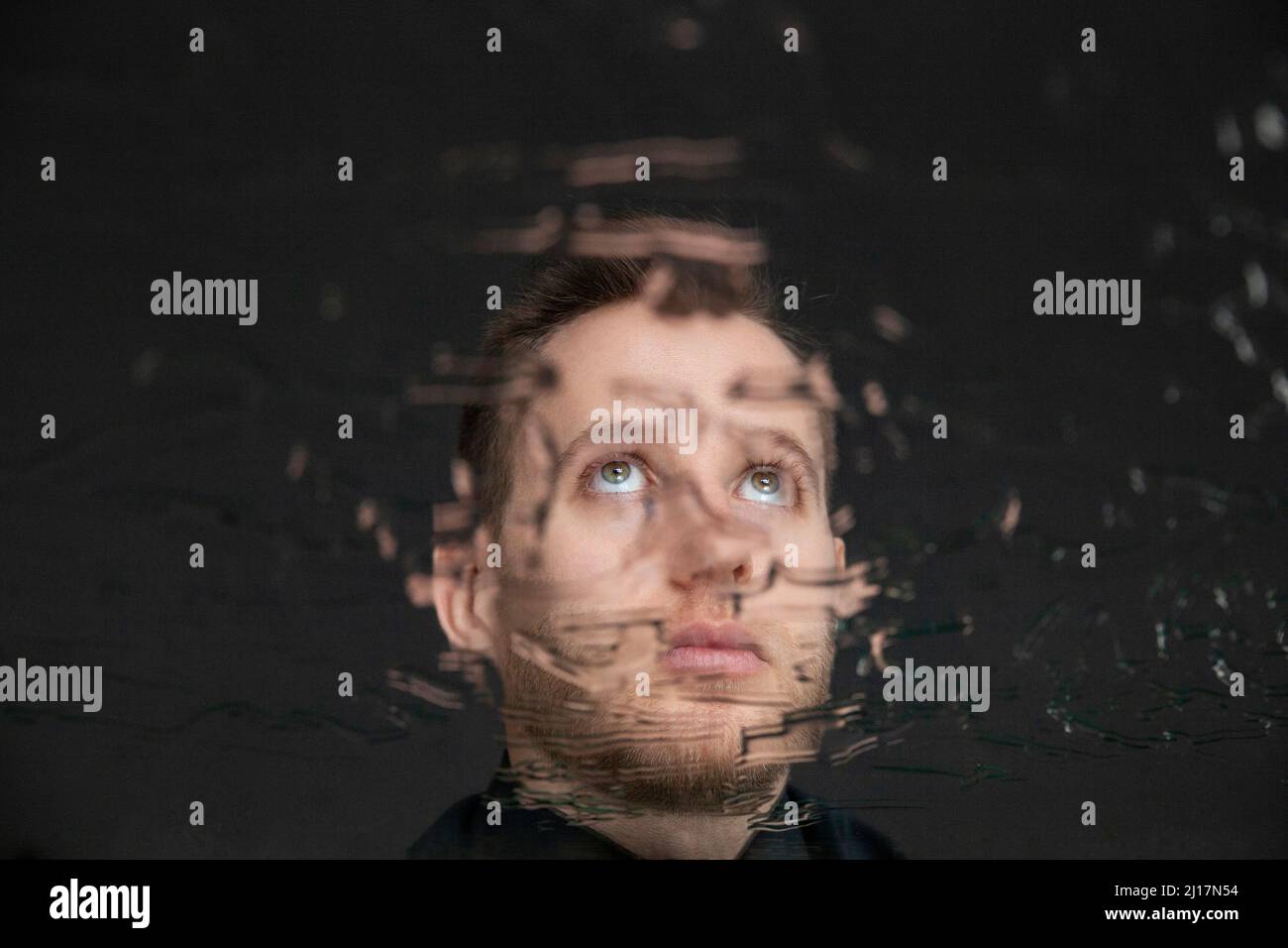 Reflection of young man on mirror with water against black background ...