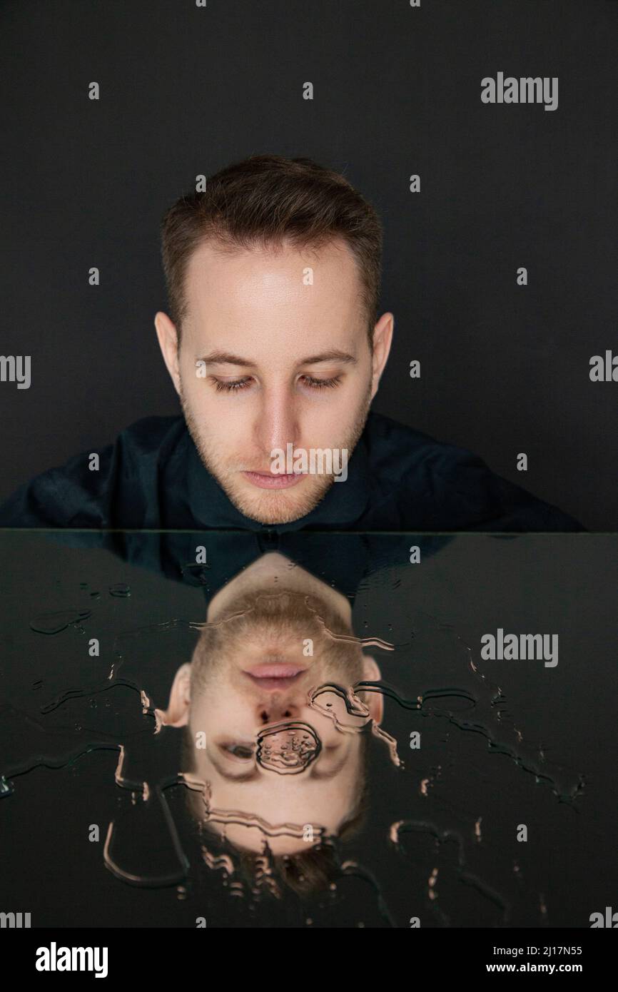 Man looking at reflection with water on mirror against black background ...