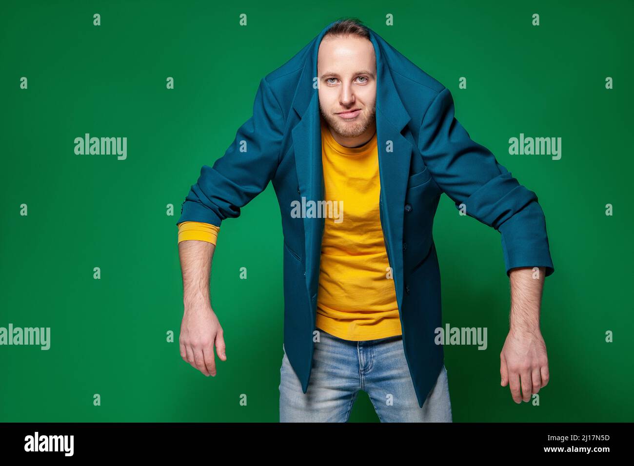 Playful young man making face standing in front of green background ...