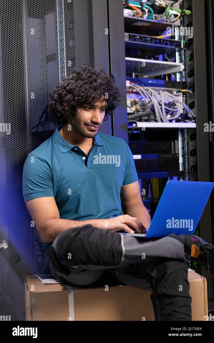 Computer programmer using laptop sitting on box in server room Stock ...