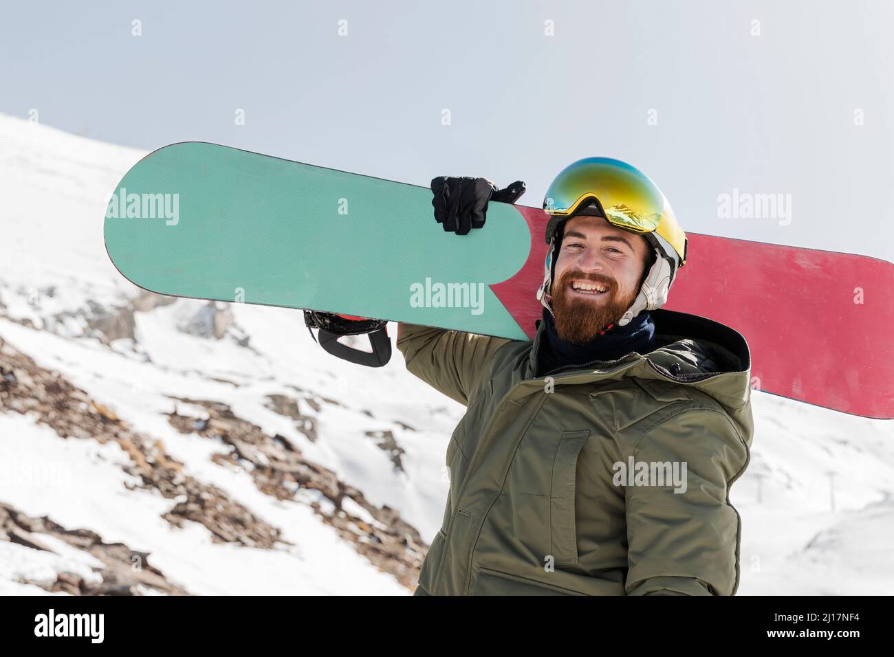 Happy young man with beard carrying snowboard on shoulder Stock Photo ...