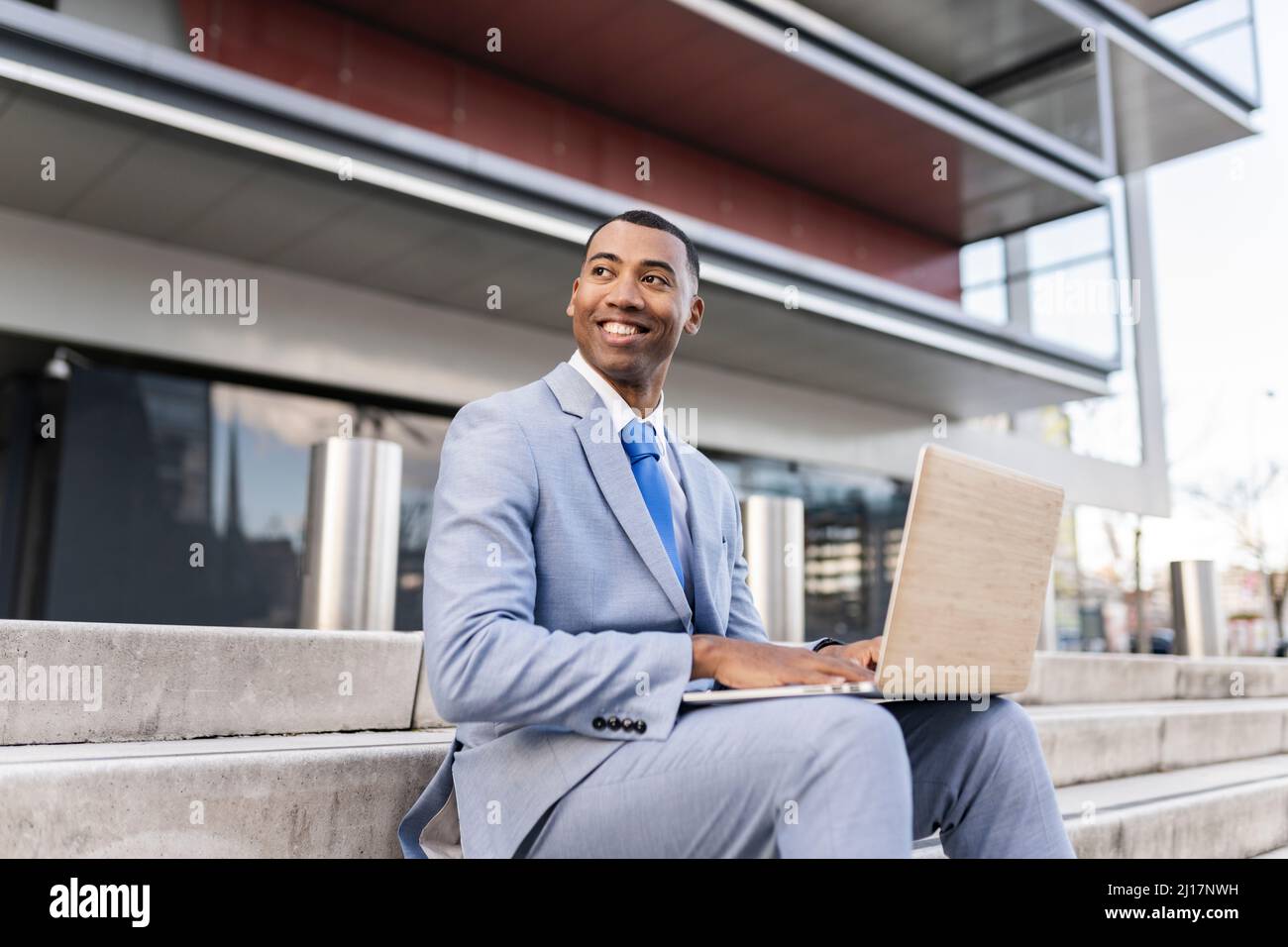 Happy businessman with laptop sitting on steps in front of building ...
