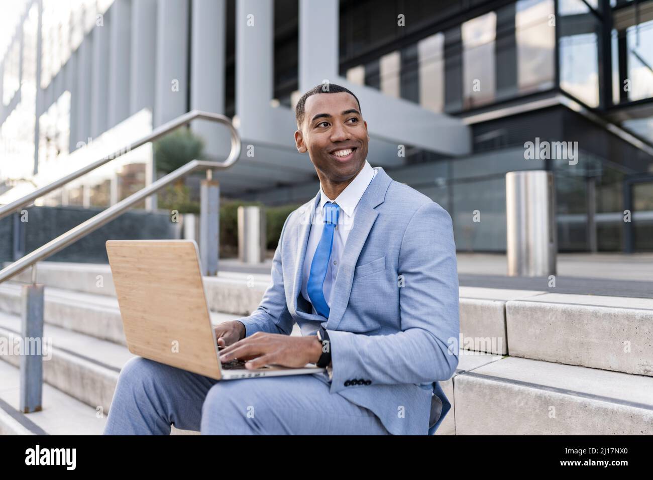 Smiling businessman with laptop sitting on steps outside building Stock ...