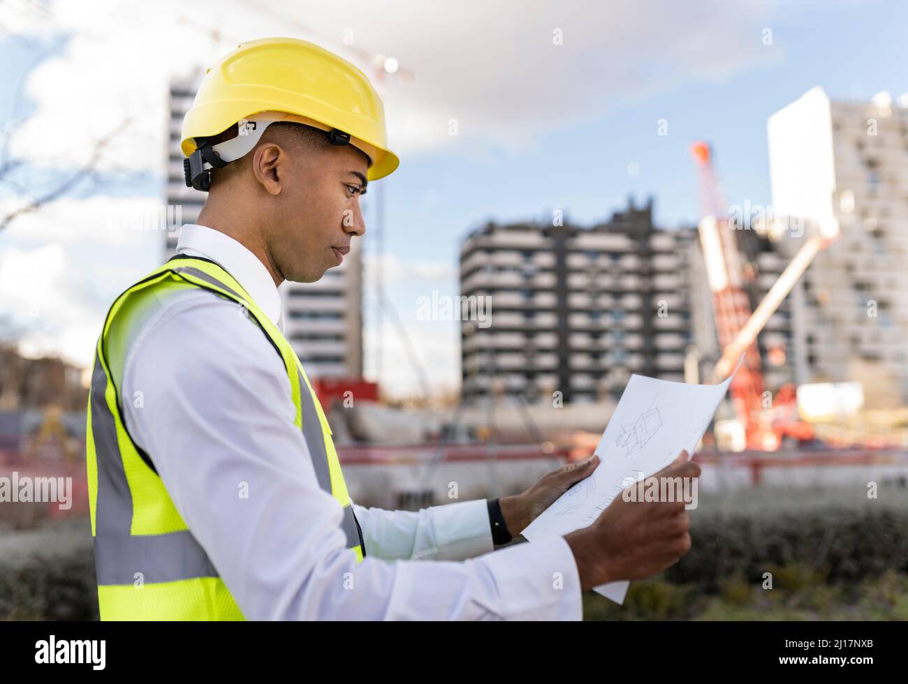 Engineer wearing hardhat reading blueprint at construction site Stock ...