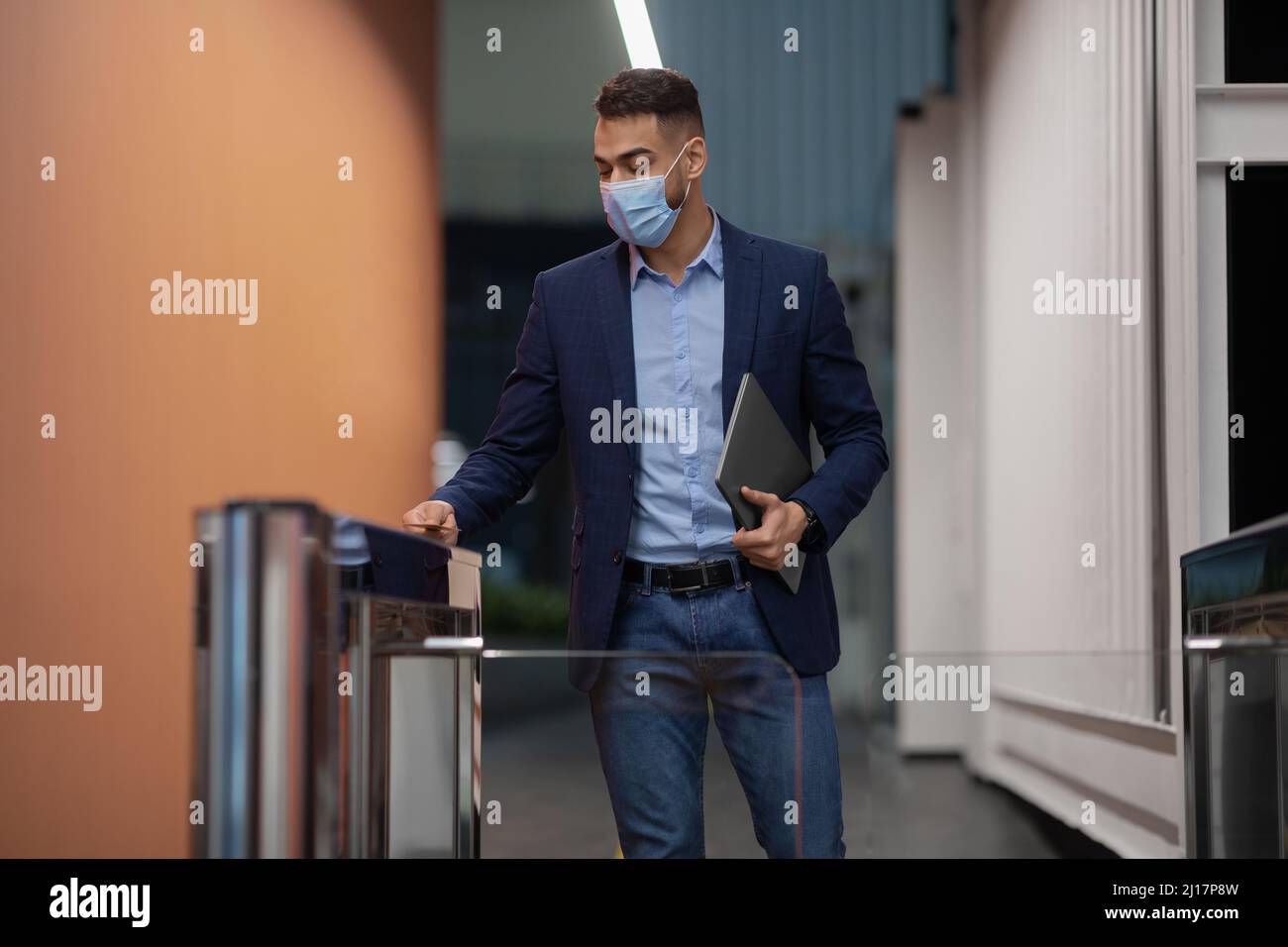 Employee in face mask holding laptop, passing through entrance gate ...