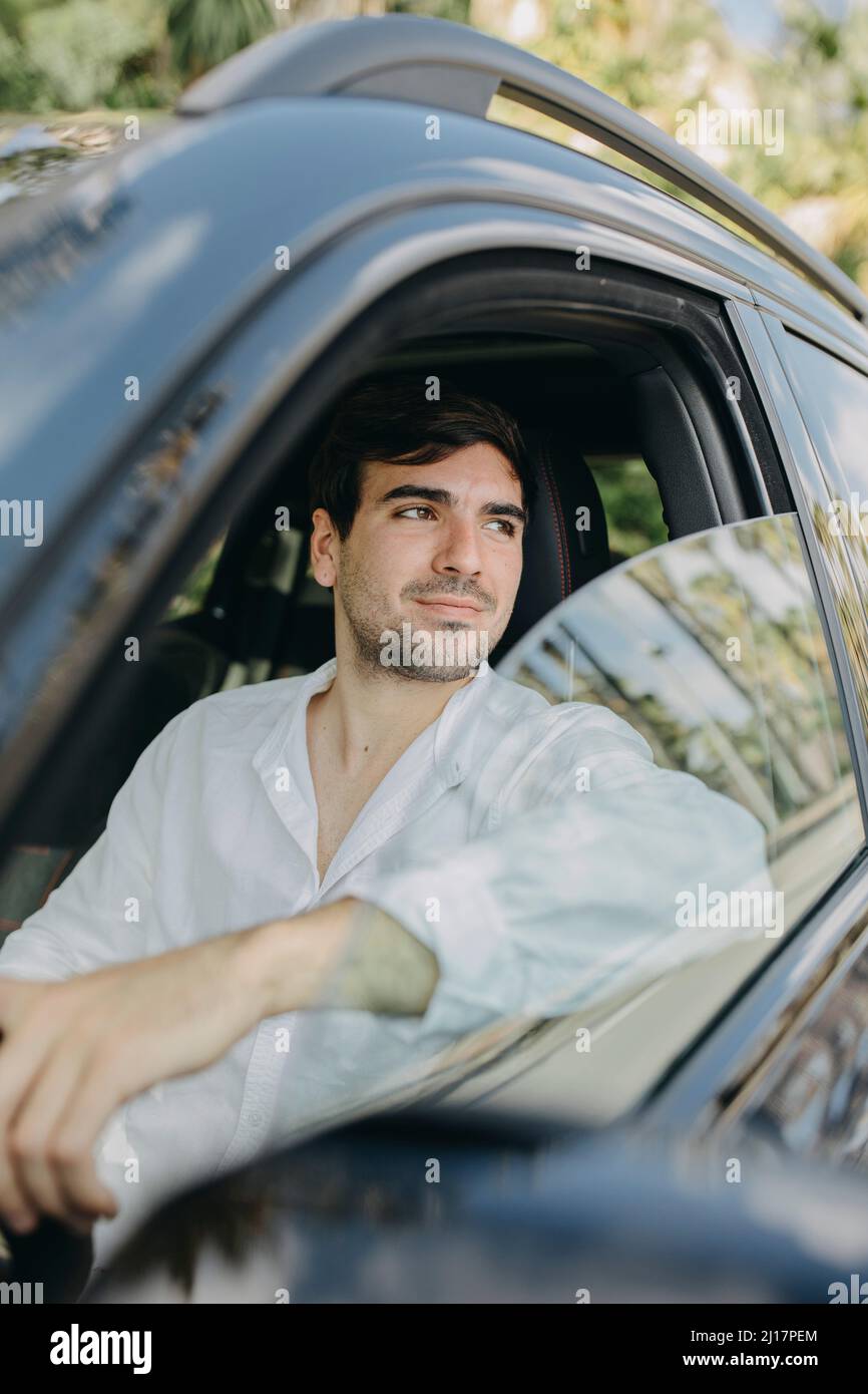 Young man looking from electric car window Stock Photo - Alamy