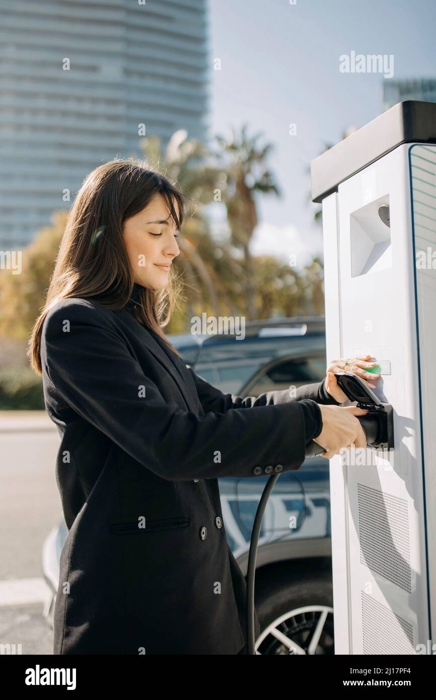 Smiling woman charging electric car at charging station Stock Photo - Alamy