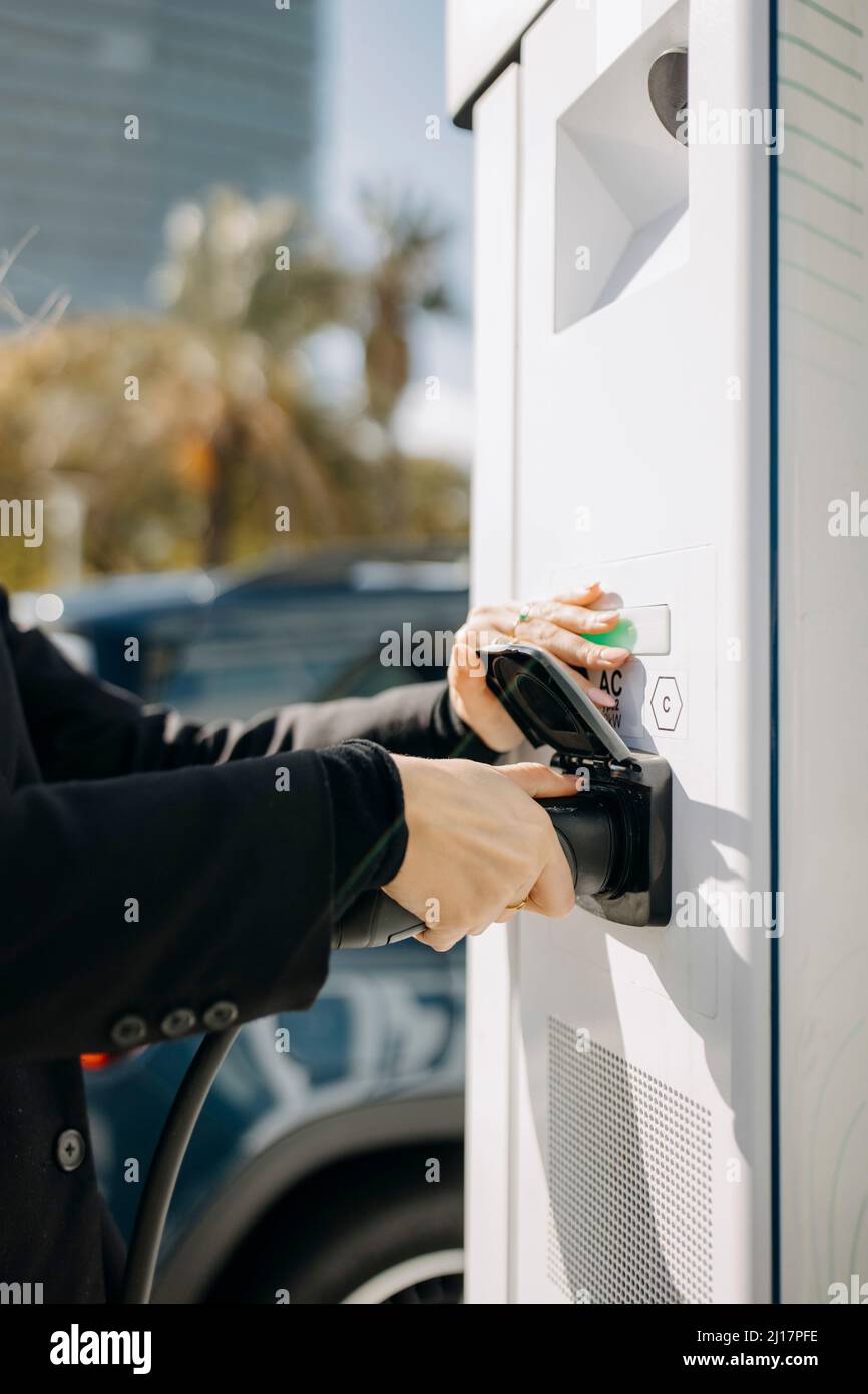Woman plugging electric car charger at charging station Stock Photo - Alamy