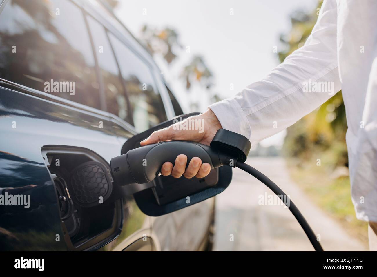 Hand of man charging electric car on roadside at station Stock Photo ...