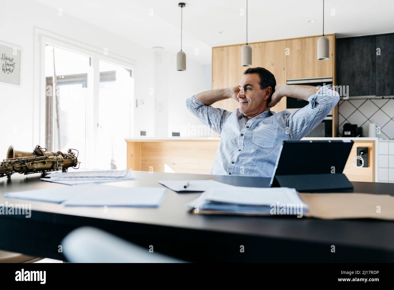 Smiling man sitting with hands behind head in kitchen at table Stock ...