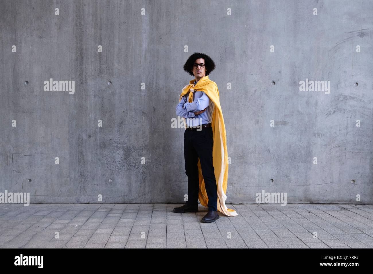 Man wearing yellow cape standing with arms crossed in front of gray ...