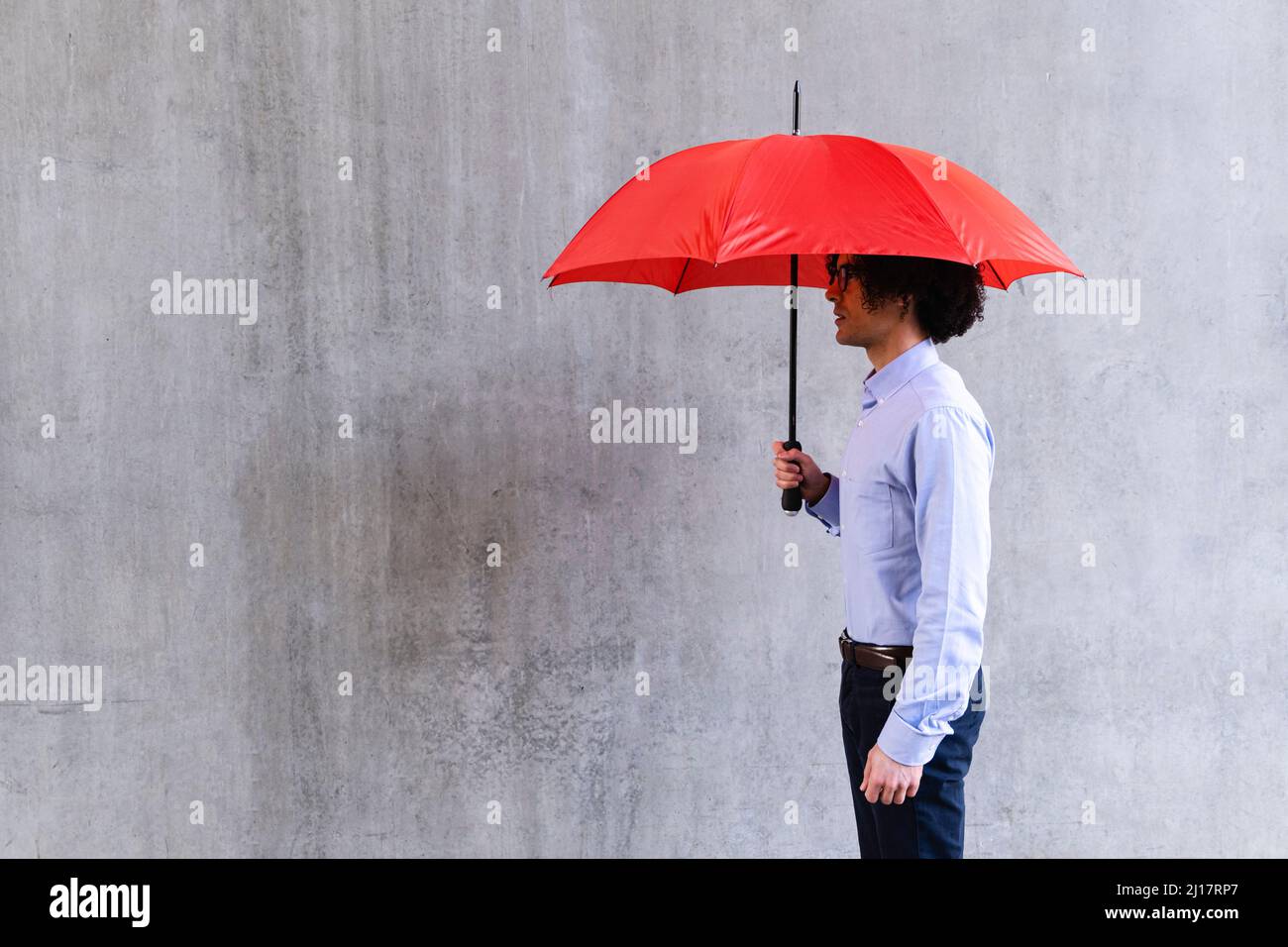 Man holding red umbrella standing in front of gray wall Stock Photo - Alamy