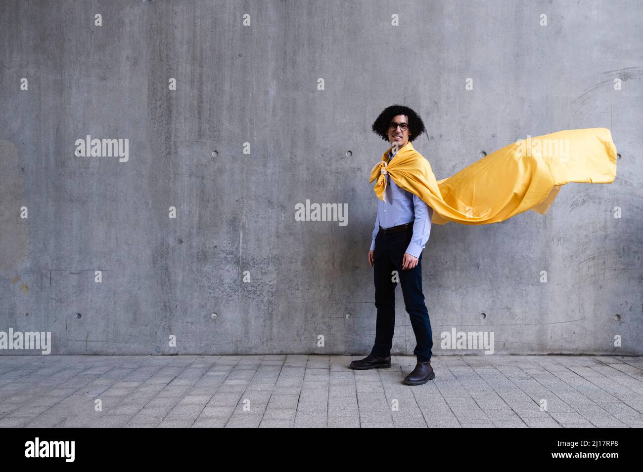 Smiling man wearing yellow cape standing in front of gray wall Stock ...