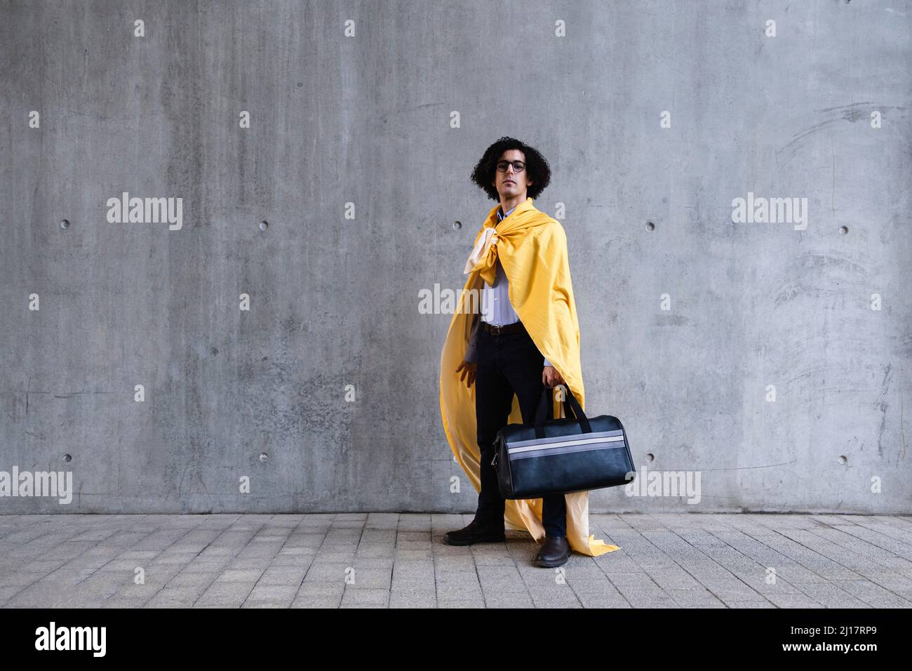 Man wearing yellow cape holding bag standing in front of gray wall ...