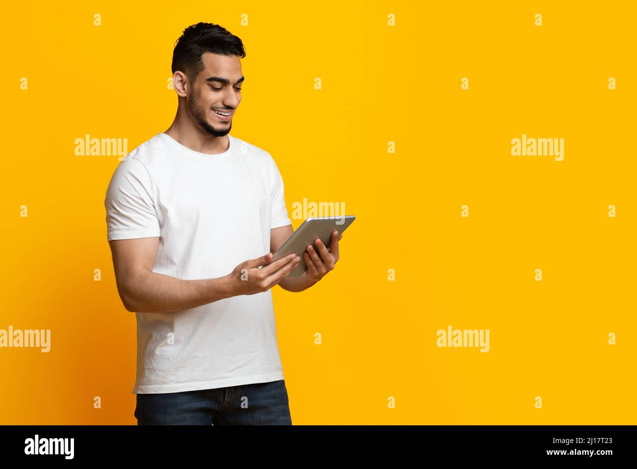 Cheerful arabic guy using digital tablet, yellow studio background ...