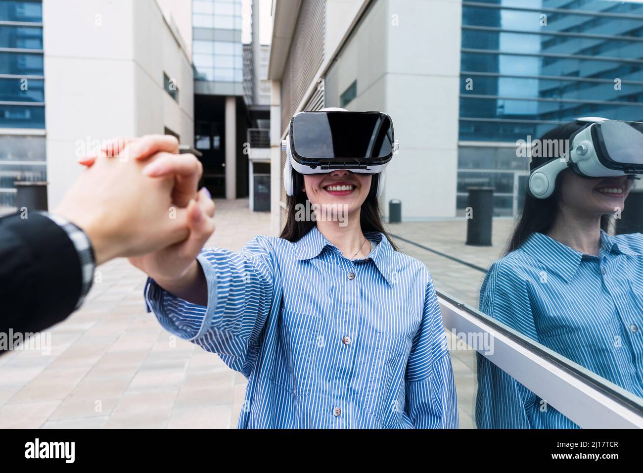 Smiling woman wearing virtual reality simulator holding hand of ...