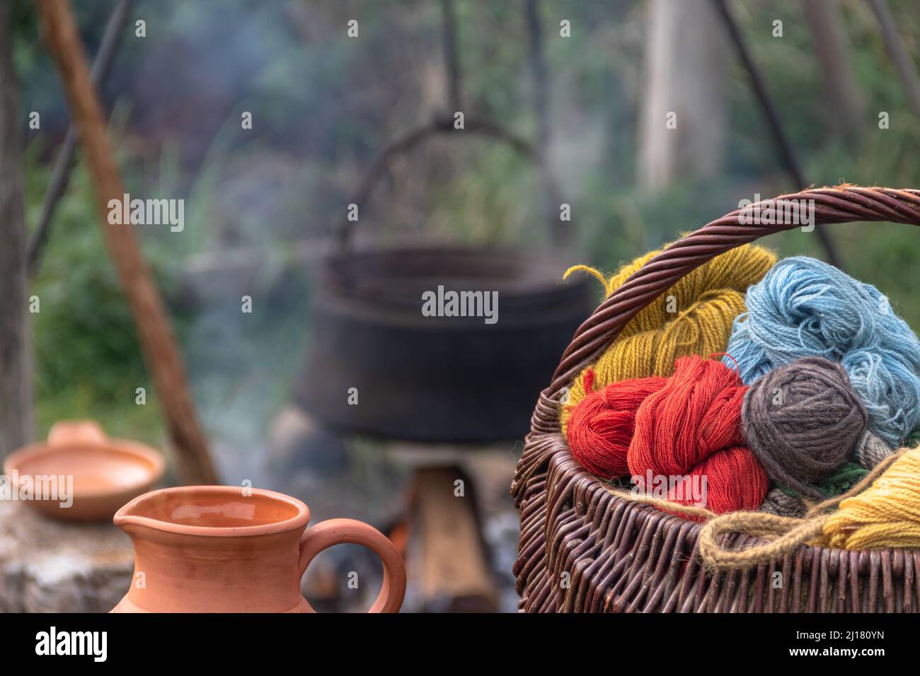 The colorful yarns in a basket next to a clay jug in an outdoor cooking ...
