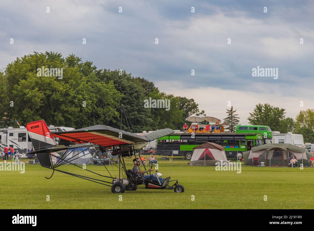 A male sitting on Ultra light flying go kart taxiing in the green grass ...