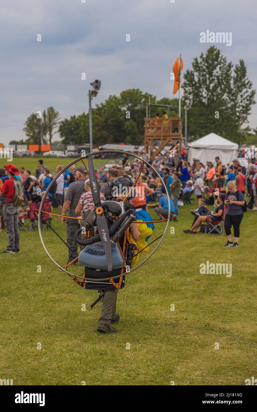 A vertical shot of male in powered paraglider walking through crowd in ...