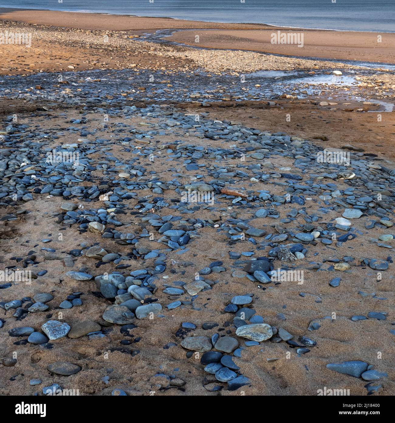 Colour photograph of coastal stones on beach smoothed and rounded by ...