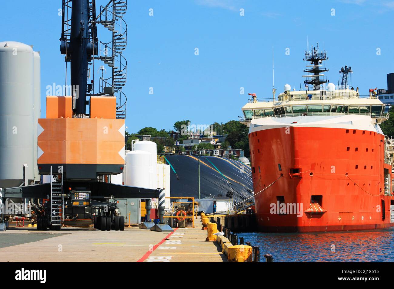 A ship moored to a pier, a large crane and fuel storage tanks on the ...