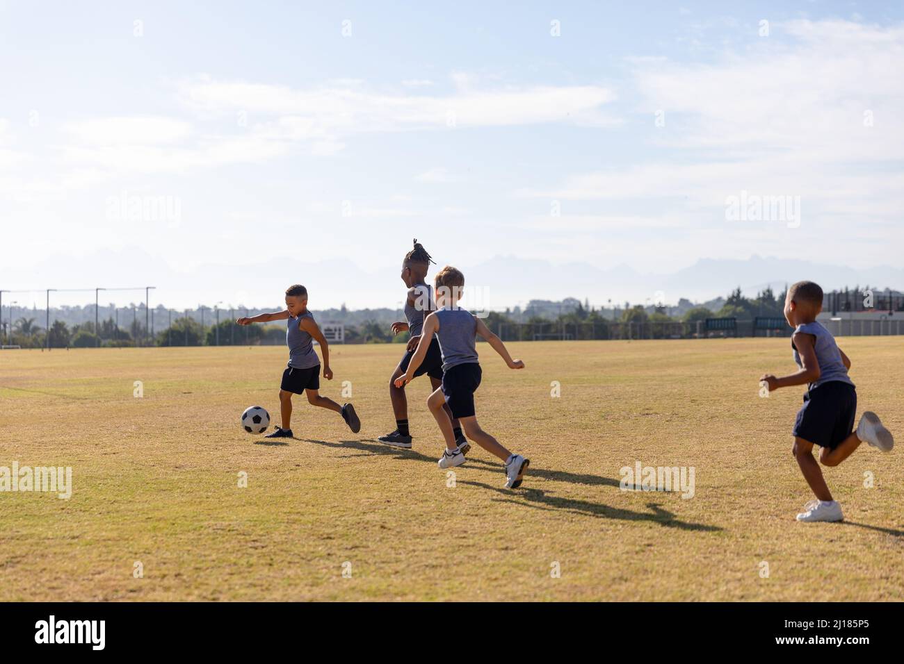 Multiracial elementary schoolboys playing soccer on school soccer field ...