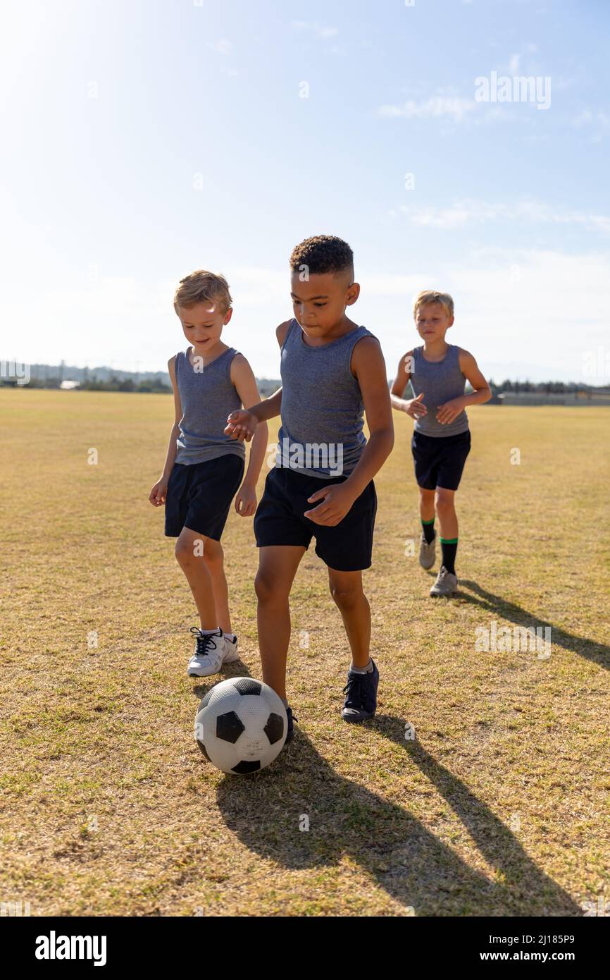 Full length of multiracial elementary schoolboys playing soccer on ...