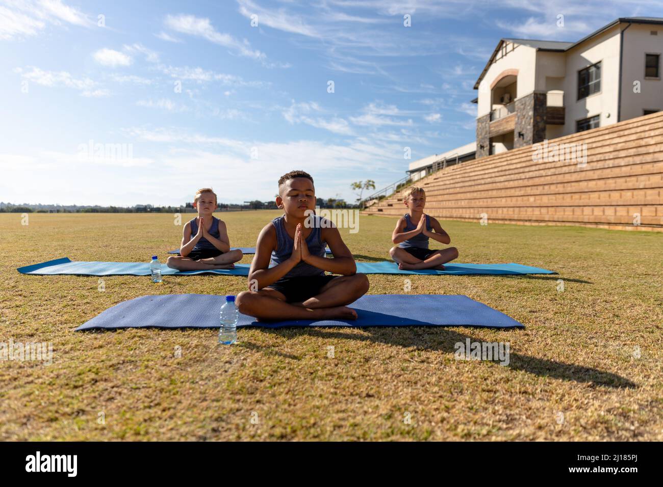 Multiracial elementary schoolboys meditating while sitting on exercise ...