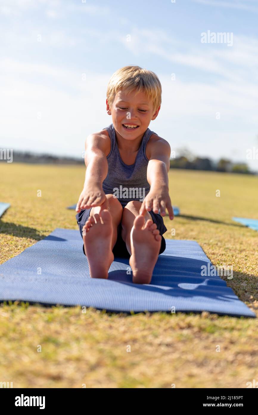 Full length of smiling caucasian elementary schoolboy touching toes ...