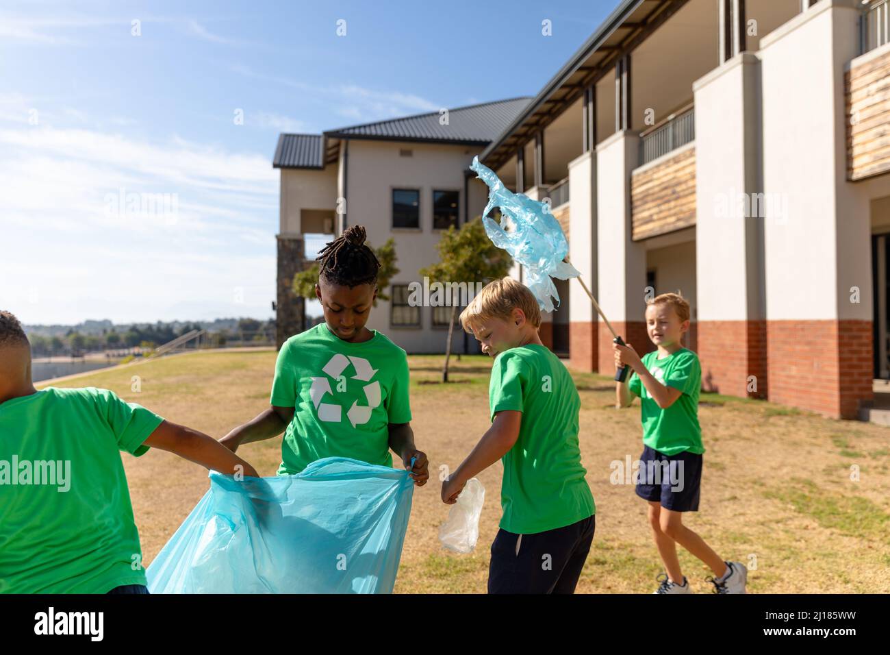 Multiracial elementary schoolboys cleaning ground by school building ...