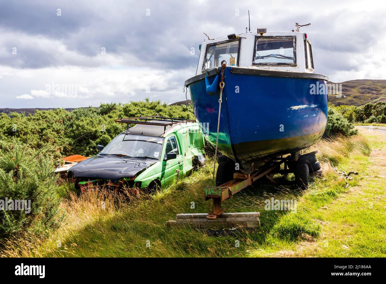 Sun shines on a boat on a trailer beside an bandoned van in countryside ...