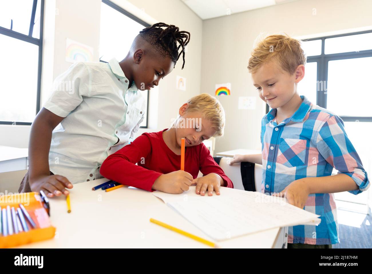 Multiracial elementary schoolboys looking at male classmate writing on ...
