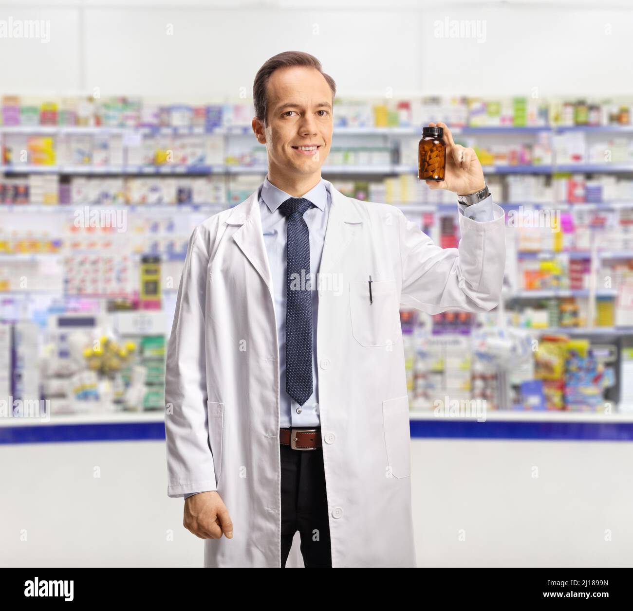 Male pharmacist showing a bottle of pills and looking at camera inside ...