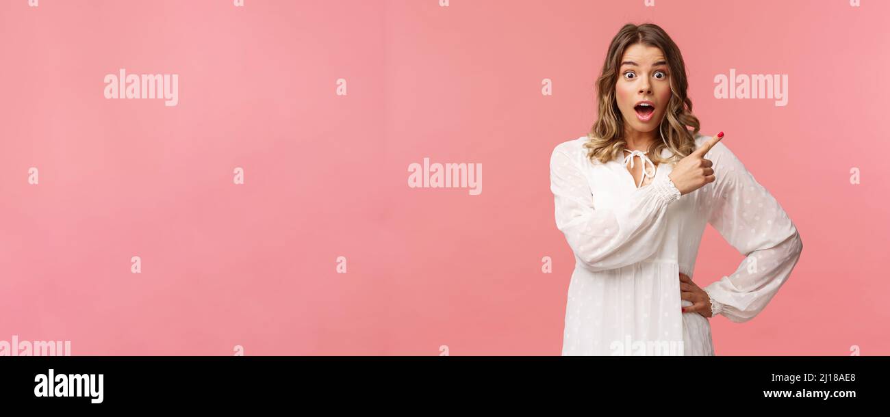 Surprised beautiful blond girl pointing upper right corner, gasping ...